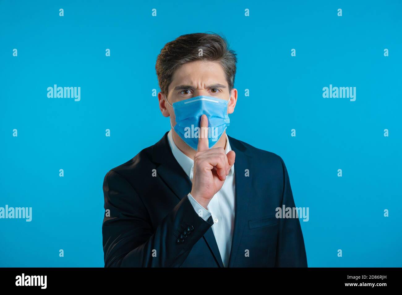 Serious business man in professional suit and mask holding finger on ...