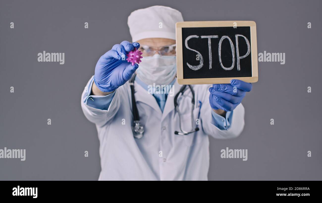 Male doctor in medical uniform shows covid-19 virus cell, stop sign in ...