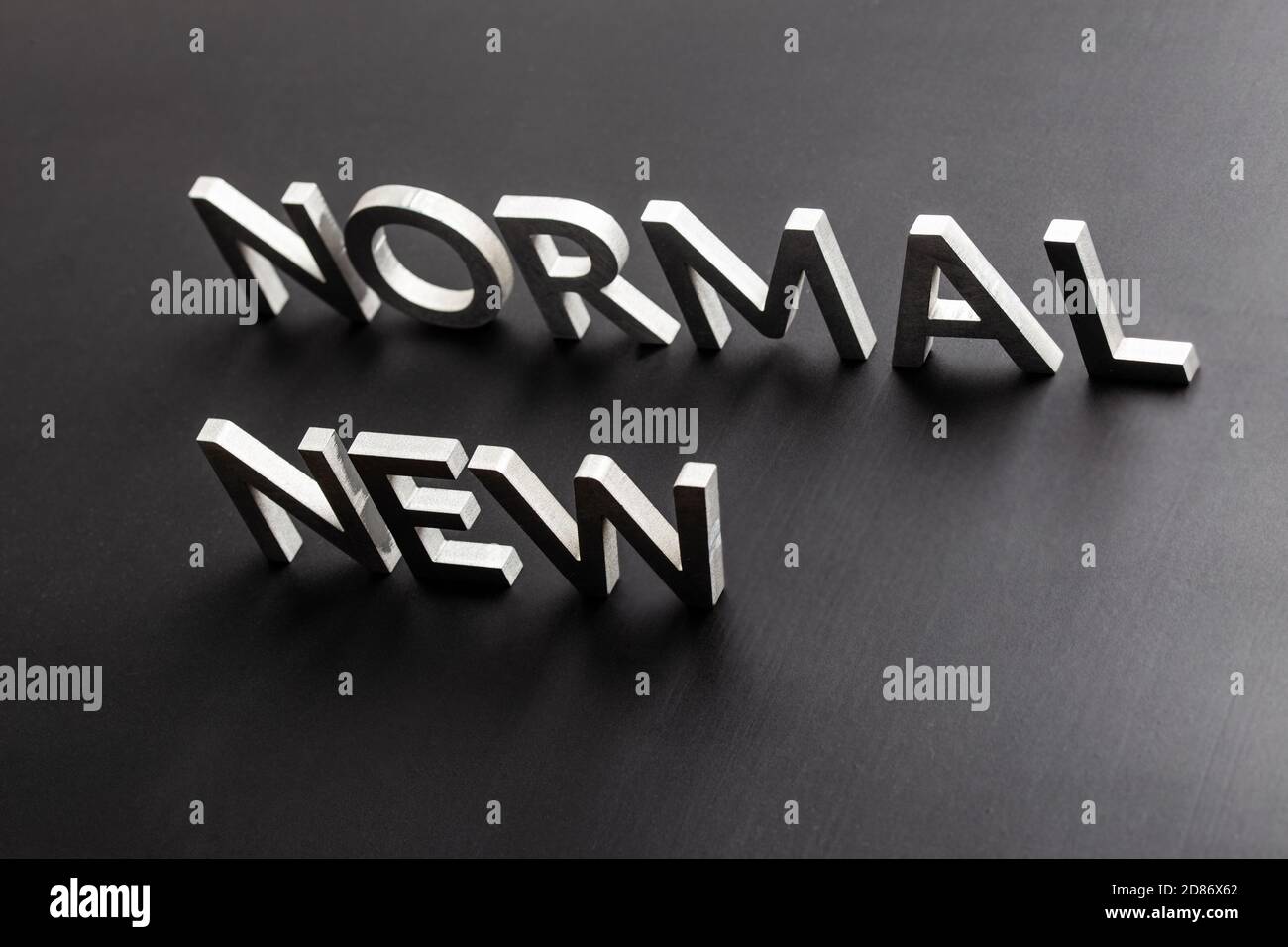 words new normal standing up on black surface in tilted linear ...