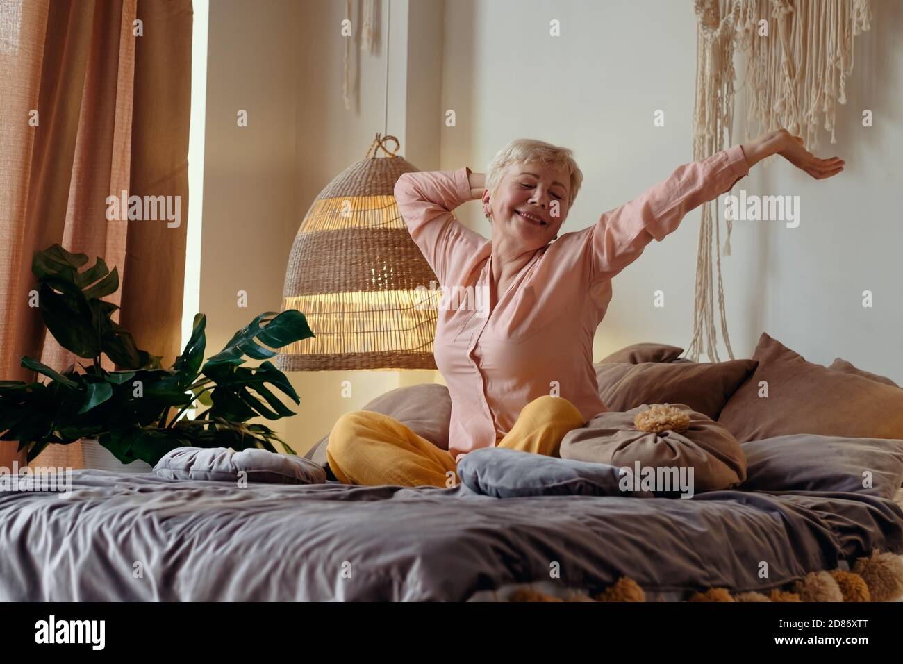 senior woman wearing pyjama smiling in bright living room stretching ...