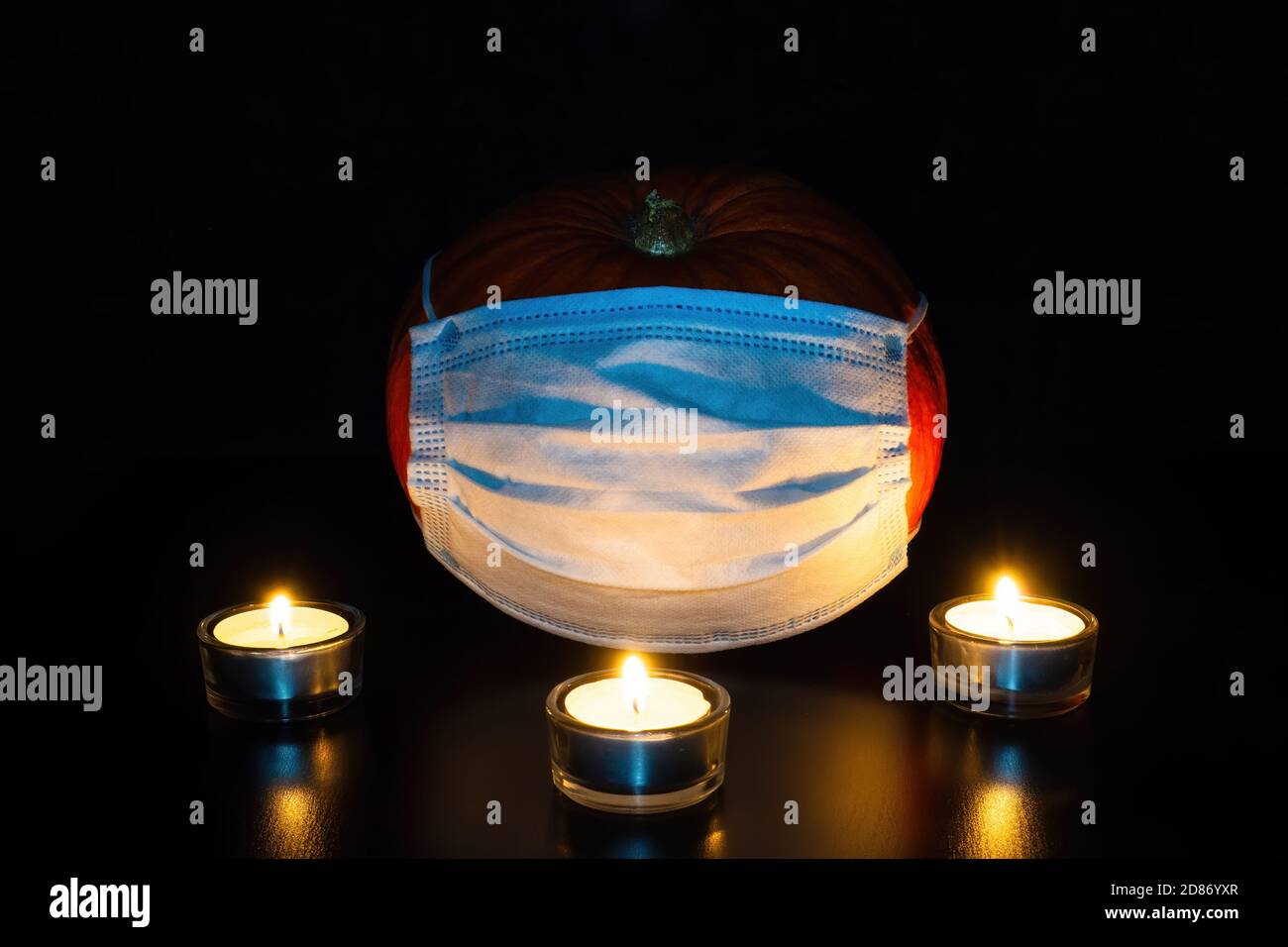 Pumpkin in medical disposable mask in dark and three lighted tea ...