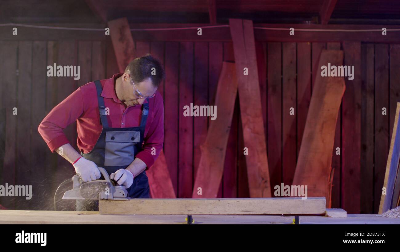 Male carpenter cleans surface of wooden beam using electric planer in ...