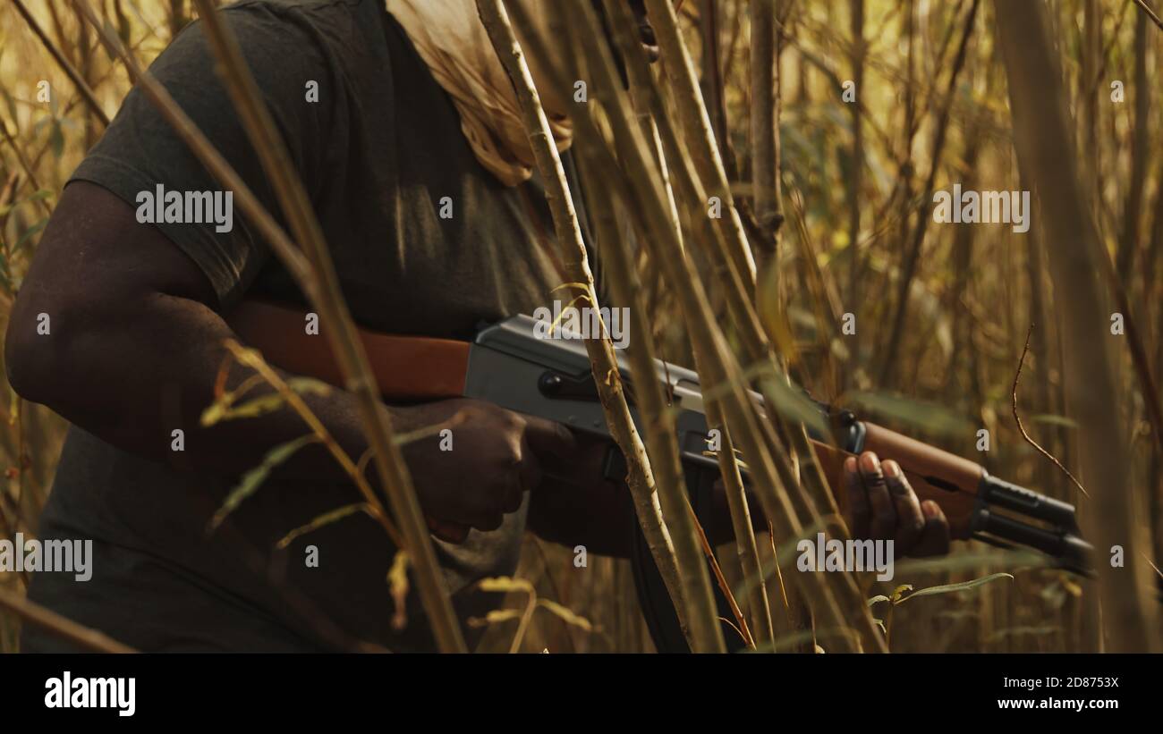 Black unrecognizable man with head covering sneaking through vegetation ...