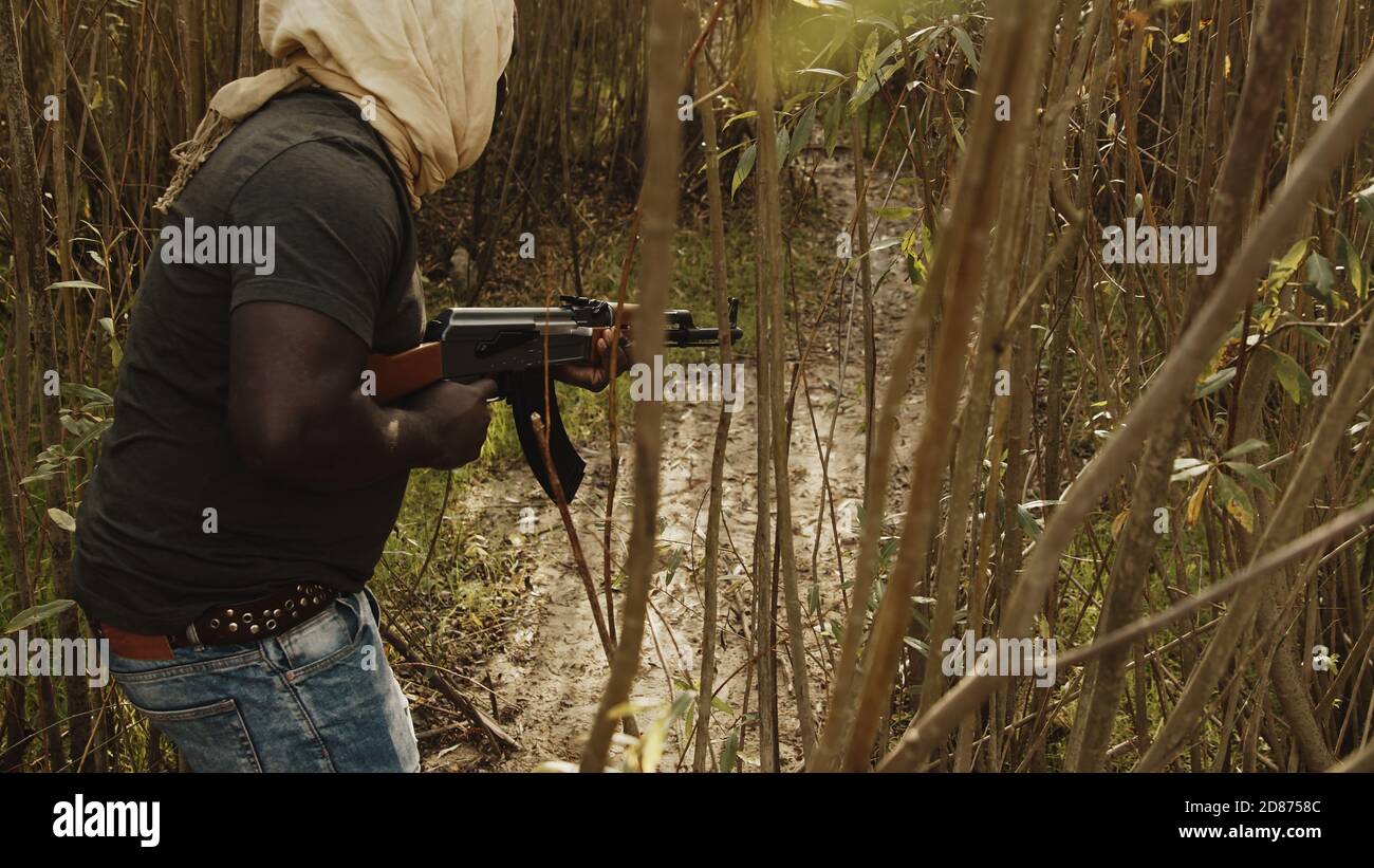 Black unrecognizable man with head covering sneaking through vegetation ...