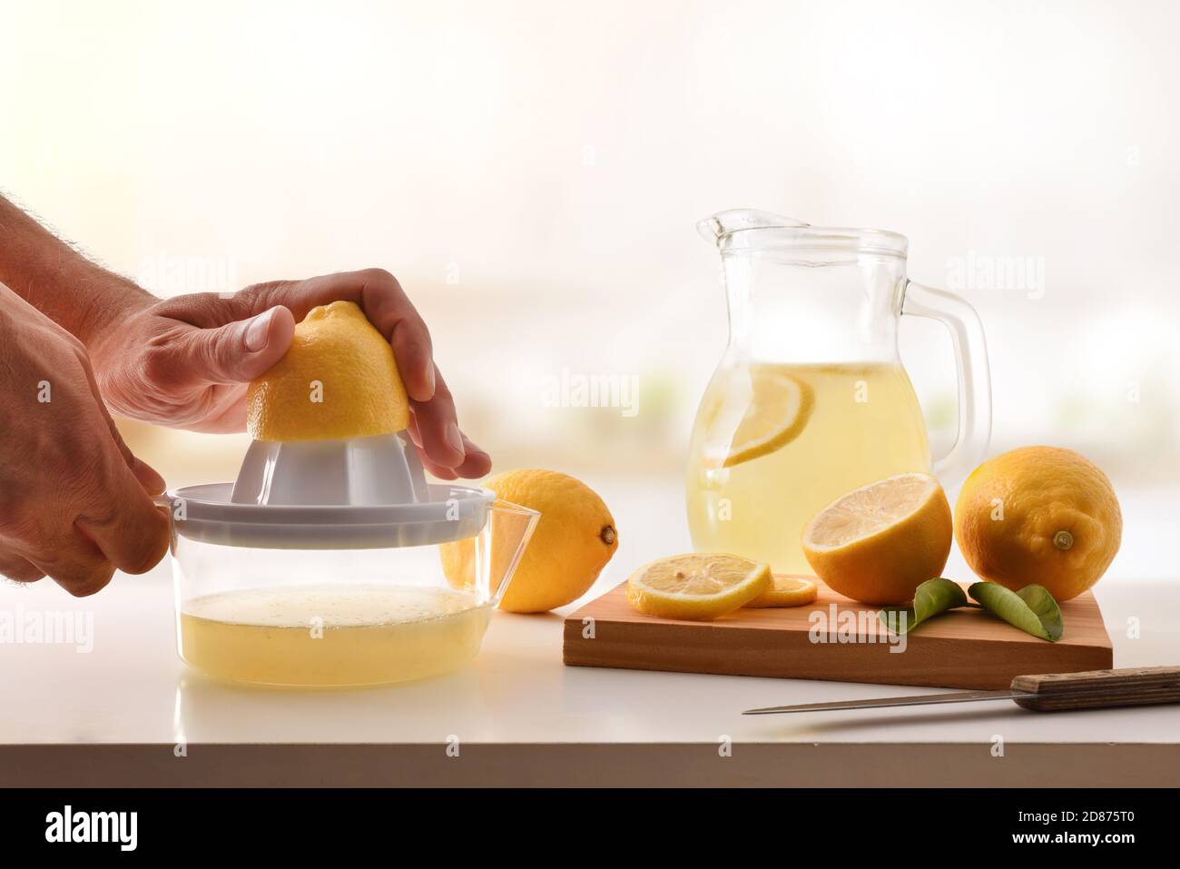 Hands squeezing a lemon in a plastic juicer with container for ...