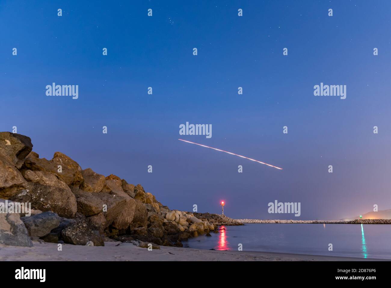 Large boulder rocks of the beach jetty line the calm reflective water ...