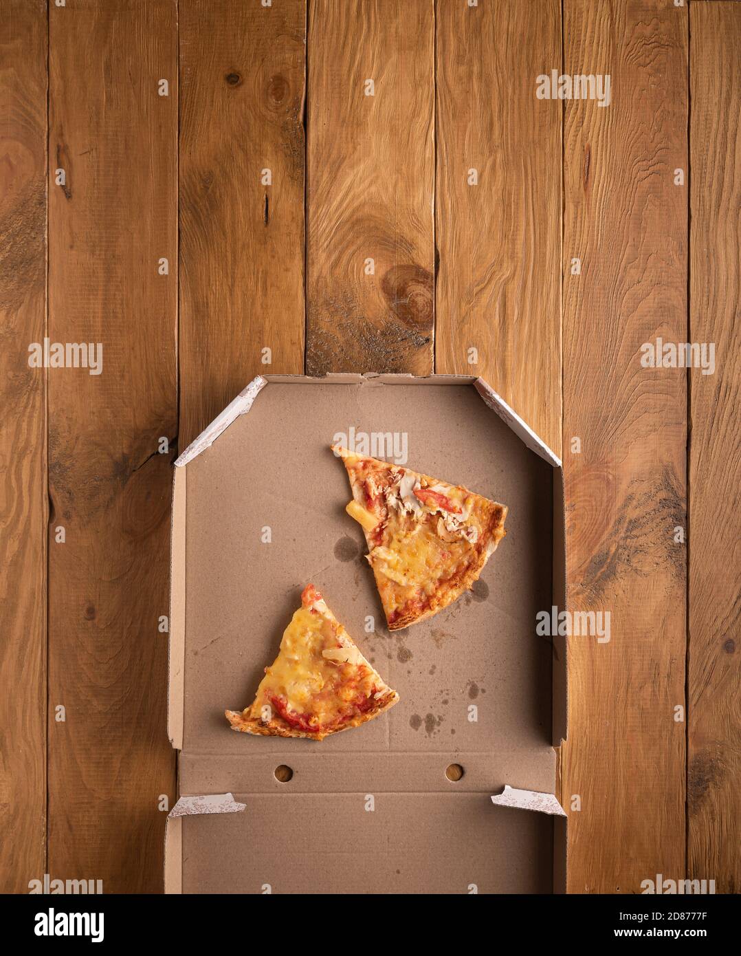 Partly visible used opened pizza box with two ugly pieces of cold pizza ...
