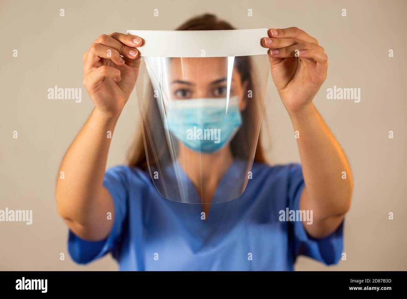 Female nurse in blue shirt holding protective face shield in front of ...