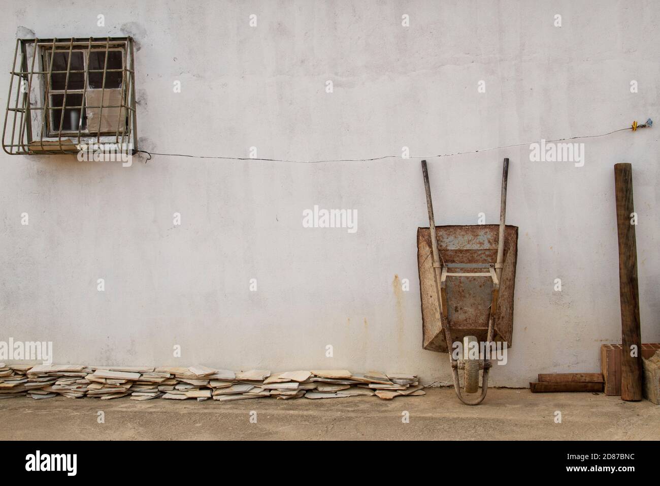 Rustic Outdoor Scene with Wheelbarrow and Window Grate on White Wall ...