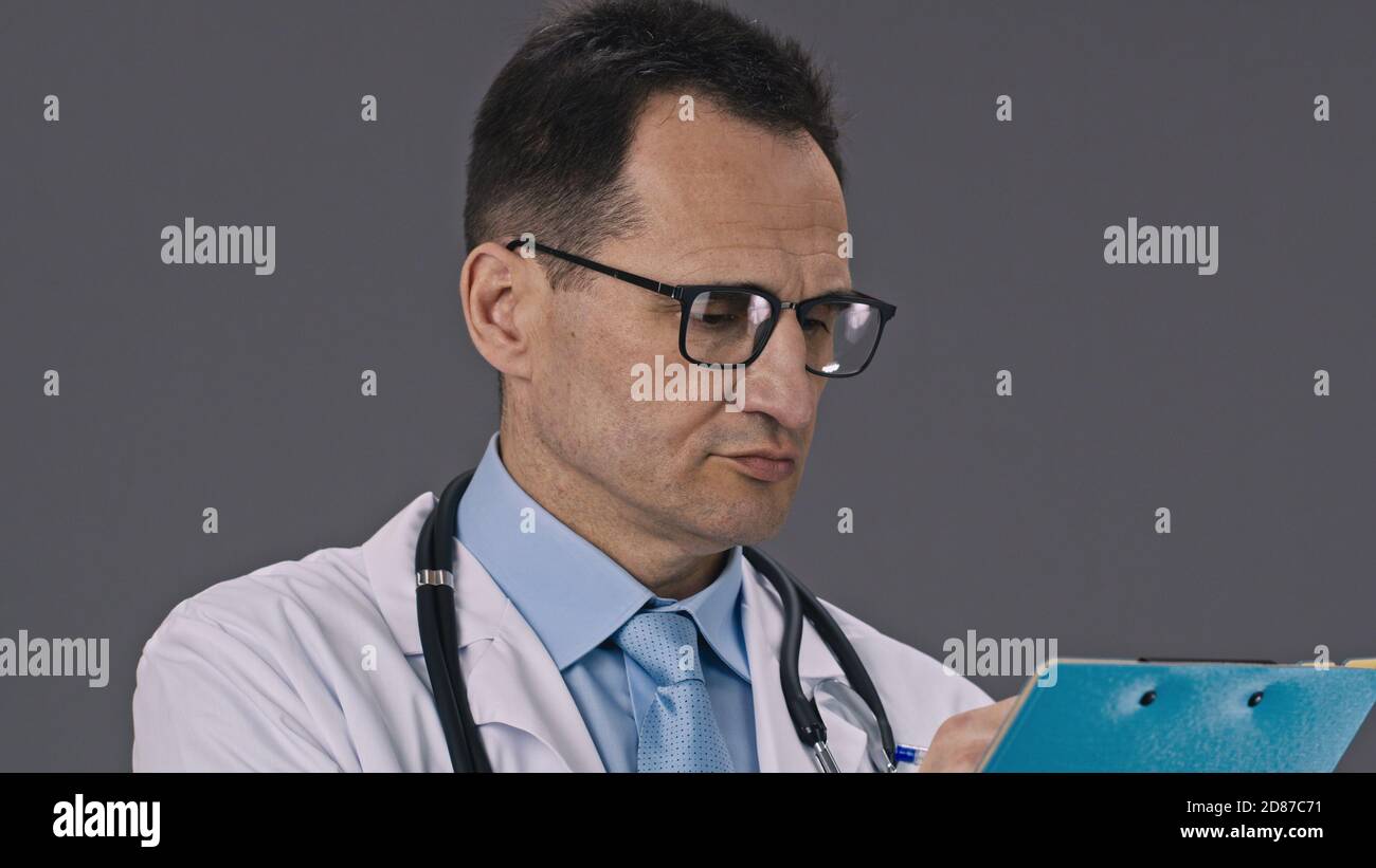 Close-up serious doctor in medical uniform writes patient diagnosis on ...