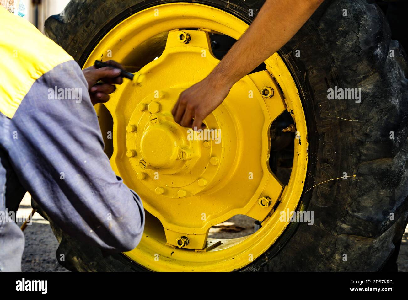 Man placing tractor wheel on yellow rim Stock Photo - Alamy