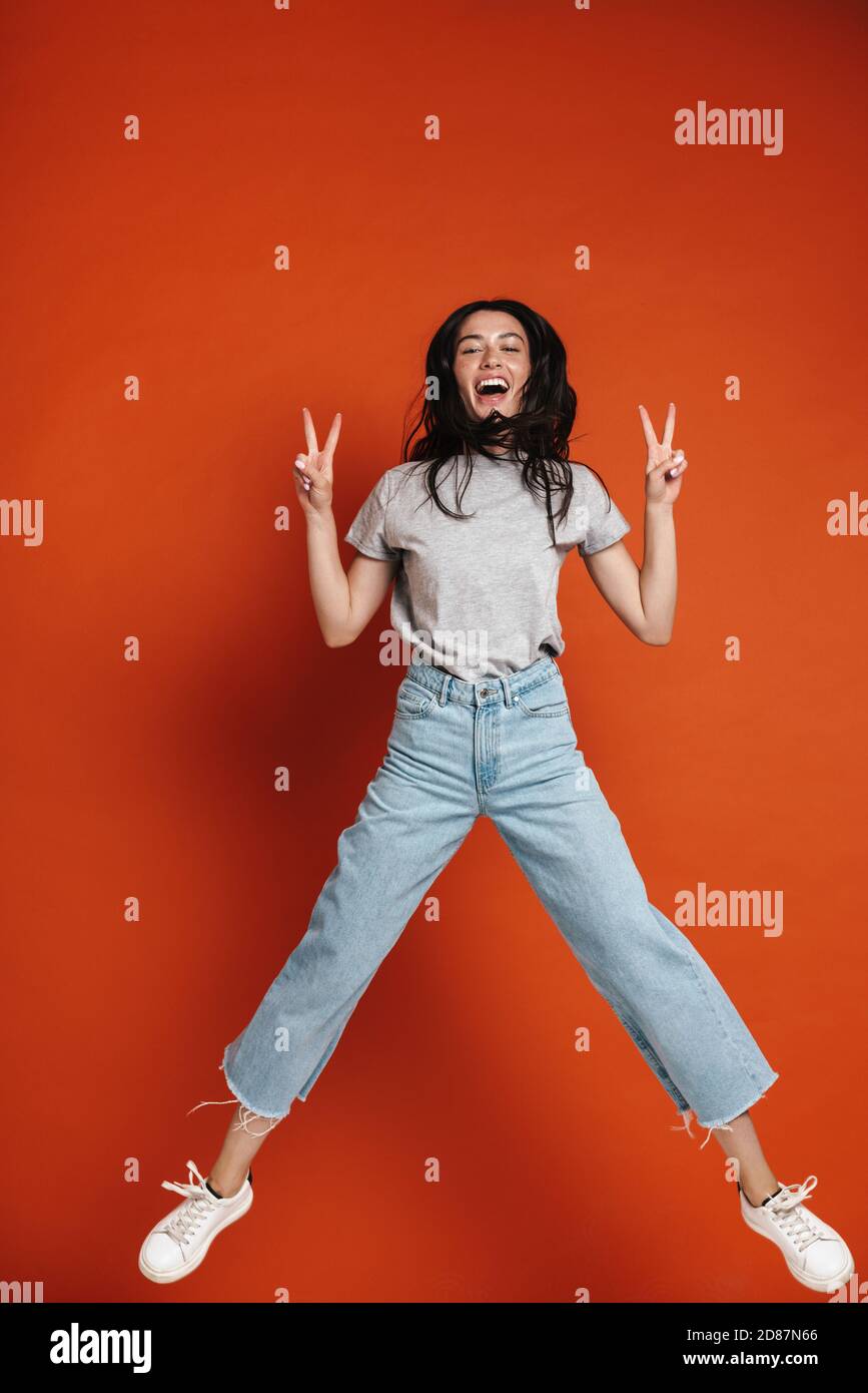 Image of young happy woman jumping and showing peace sign isolated over ...