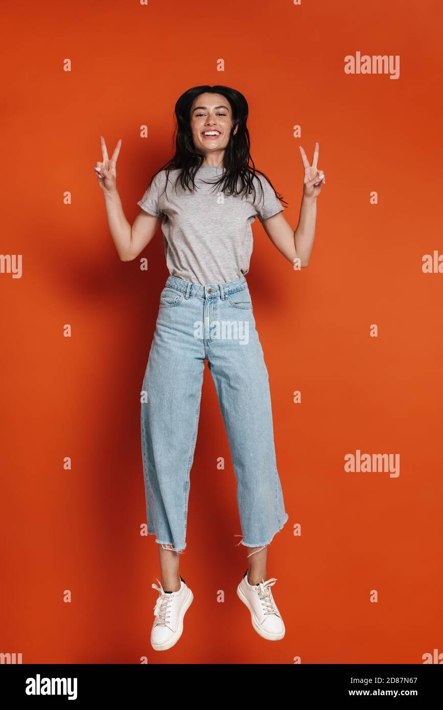 Image of young happy woman jumping and showing peace sign isolated over ...