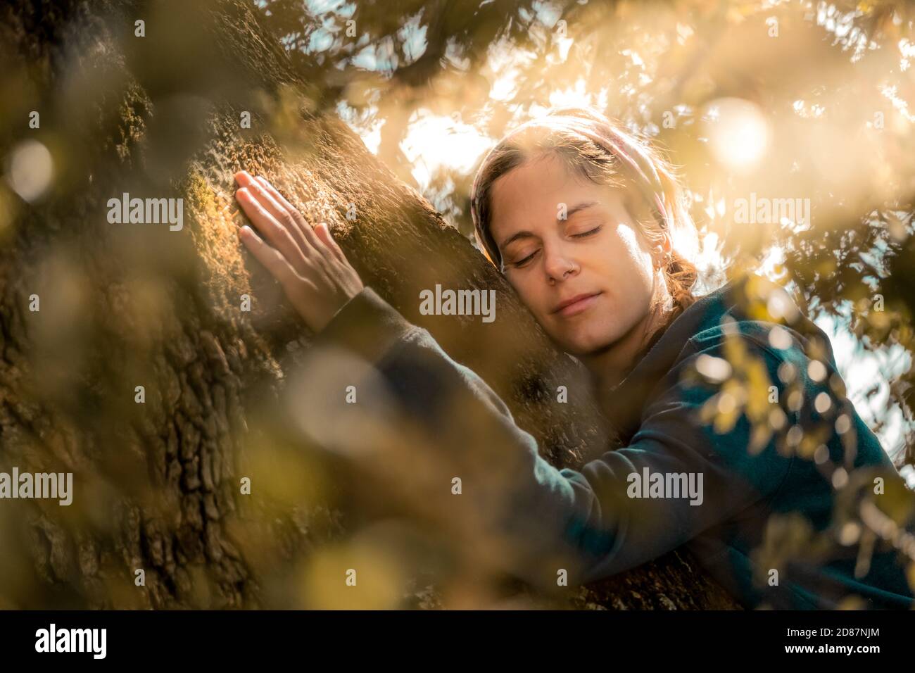 Close portrait of young woman hugging the trunk of an old oak tree with ...