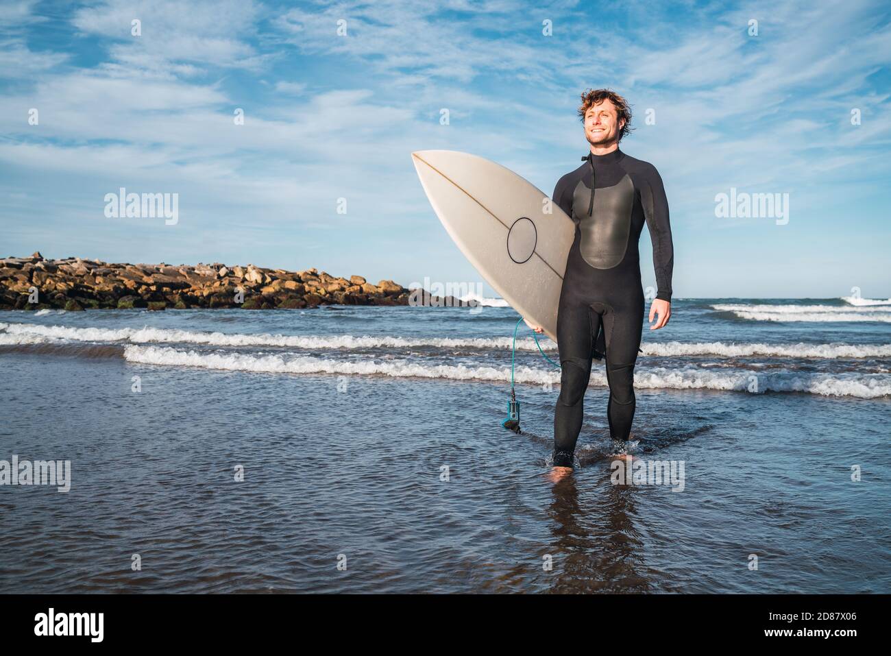 Portrait of young surfer leaving the water with surfboard under his arm ...