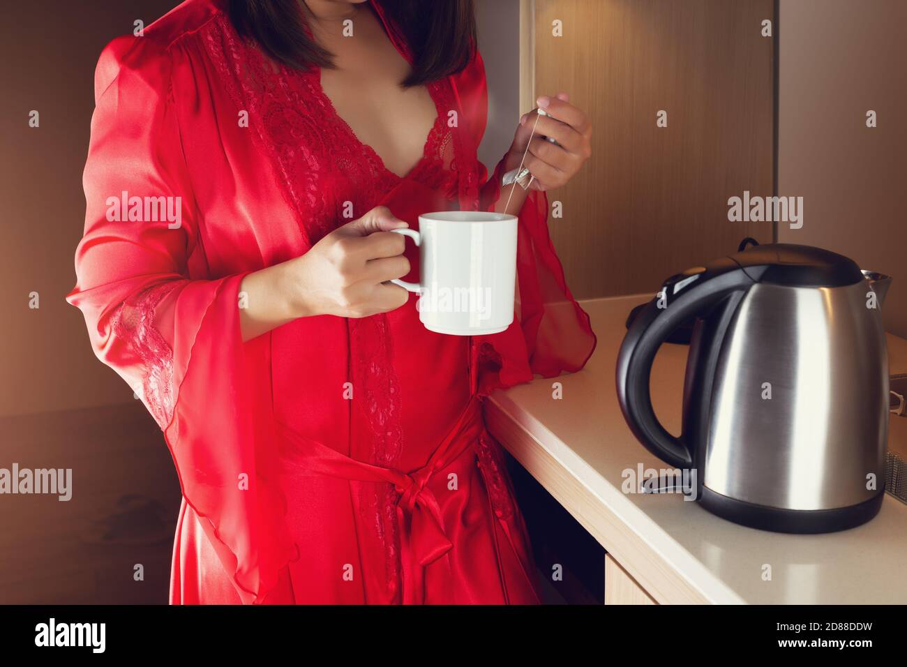 A woman in a red silk nightgown and luxurious robes making hot tea in ...