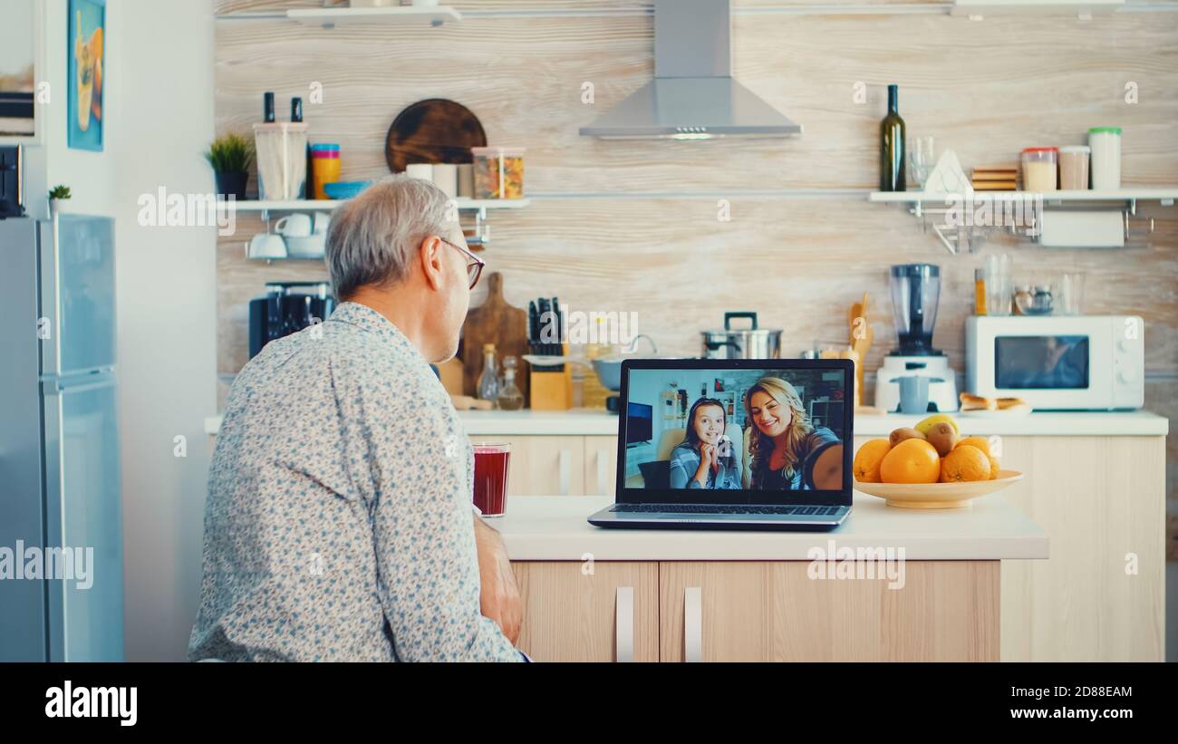 Senior man during video conference with daughter in kitchen using ...