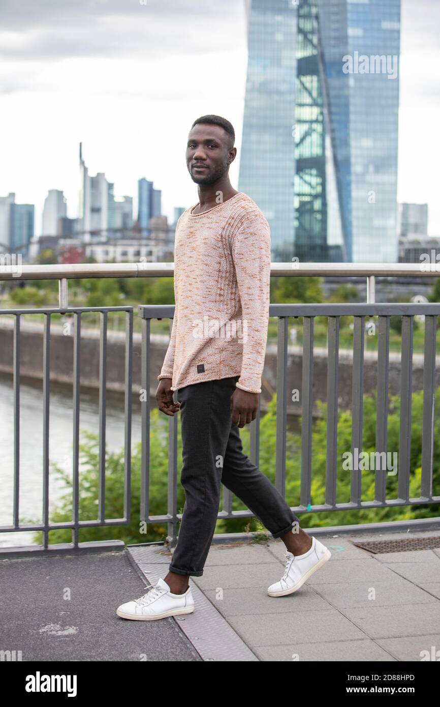 Fashionable young black man walking with head turned looking at camera ...