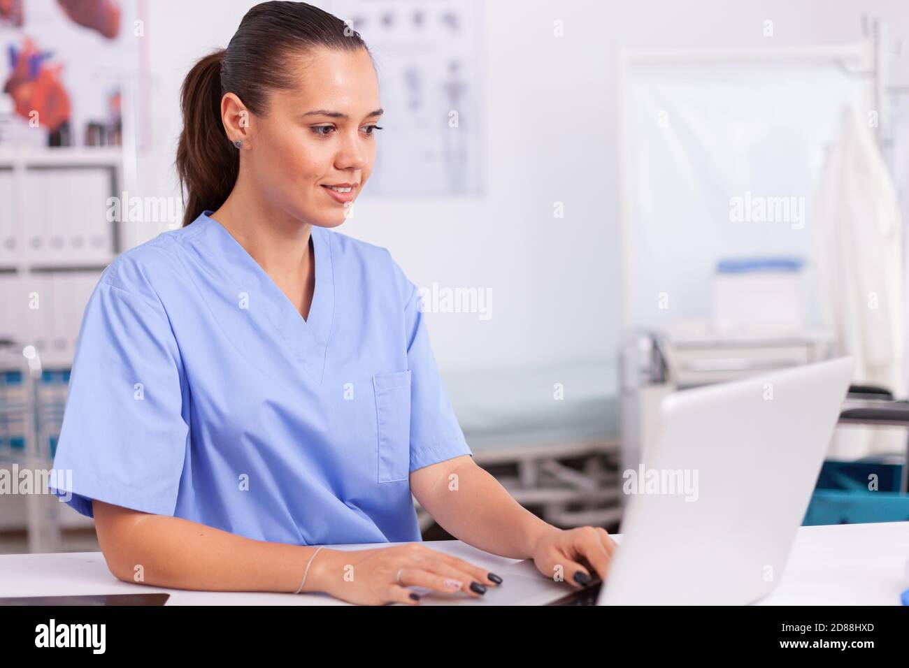 Medical physician typing on laptop sitting at desk wearing blue uniform ...