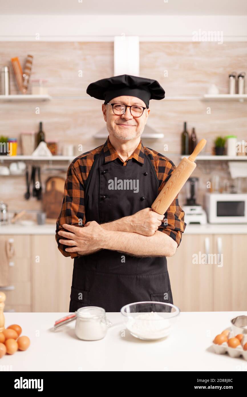 Caucasian old man wearing apron in home kitchen smiling at camera ...