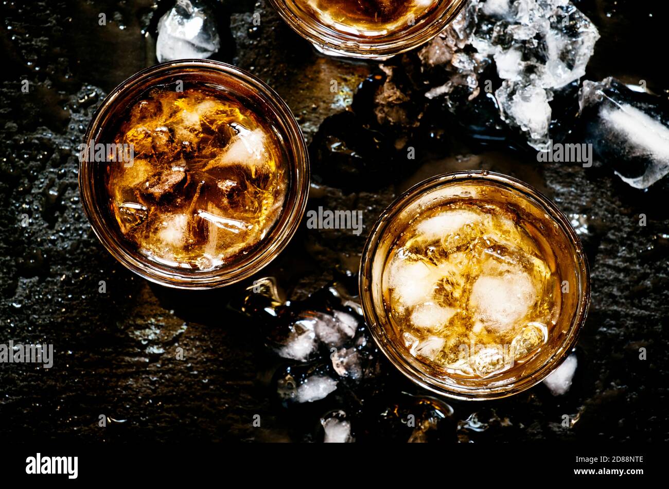 Cold whiskey in a glass with crushed ice on a black stone wet ...