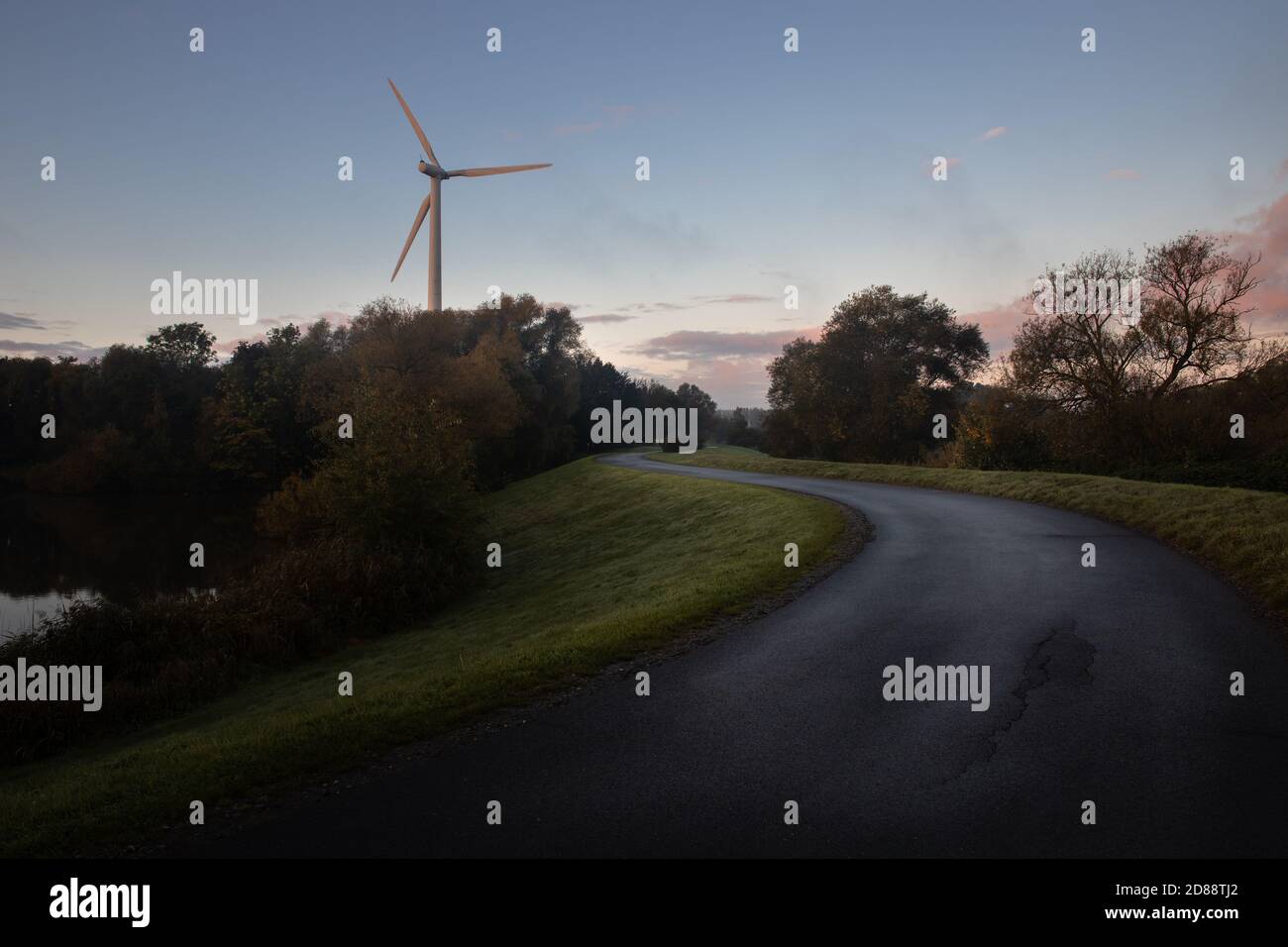 small road winding towards a wind turbine at sunrise symbolizing the ...