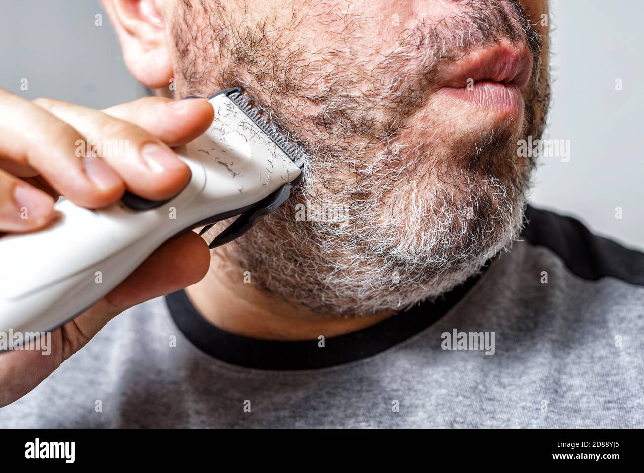 gray-haired man cuts his beard with an electric clipper Stock Photo - Alamy