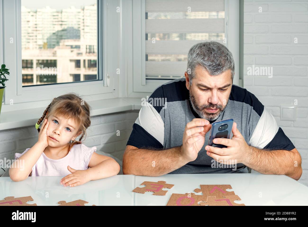 dad uses his cell phone. the little daughter is sad and waiting for her ...