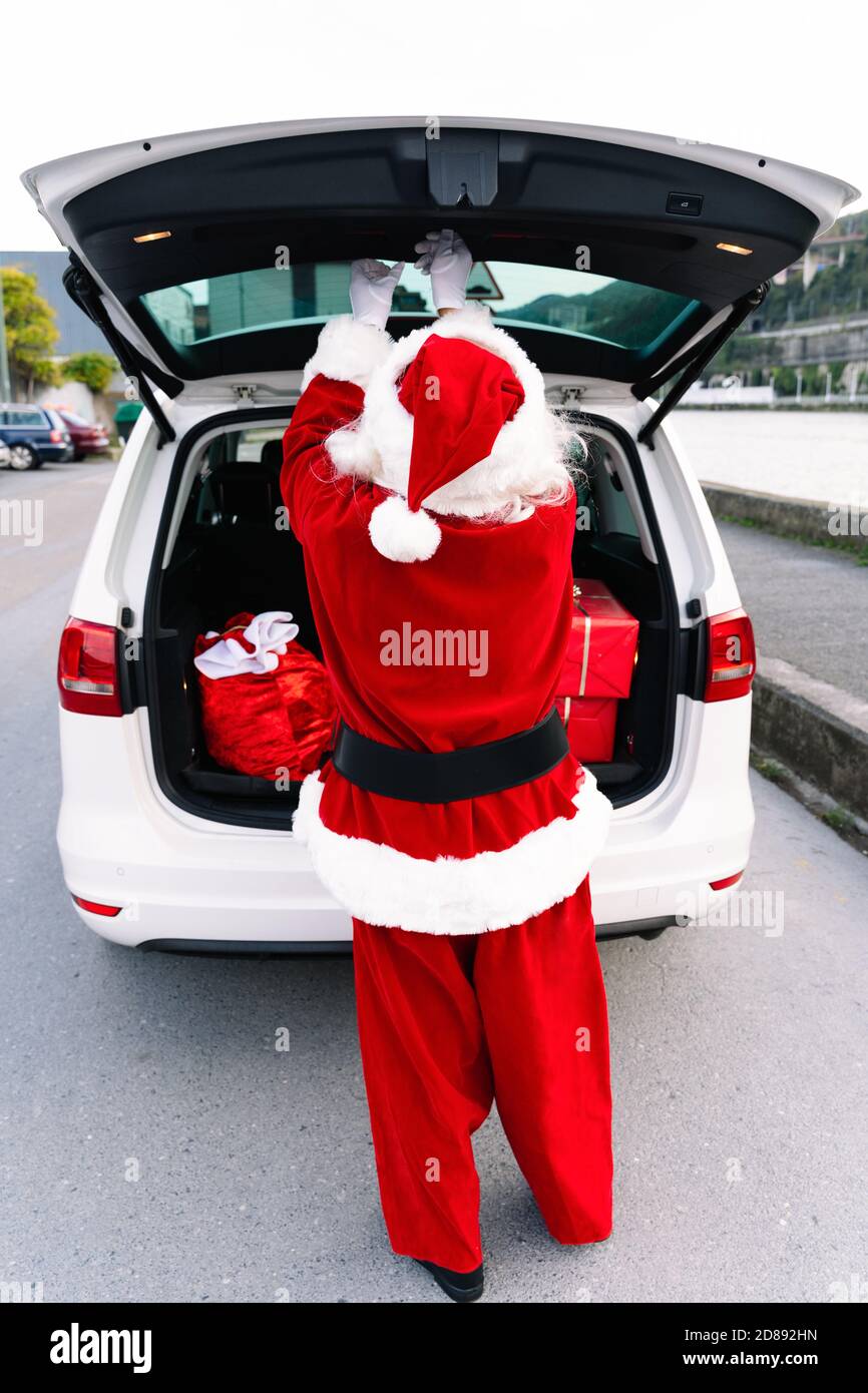 Portrait of Santa Claus with the trunk of the car open full of gifts ...
