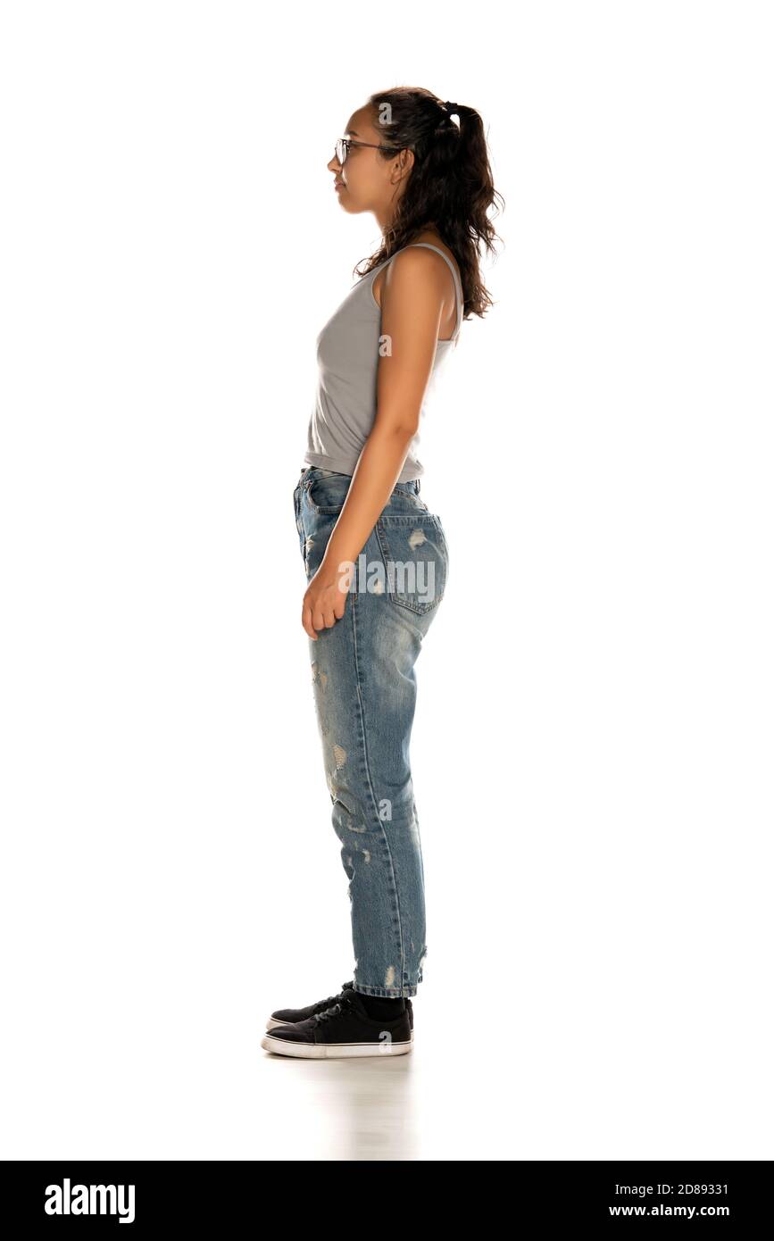 Side view of young dark skinned woman in jeans standing on white ...