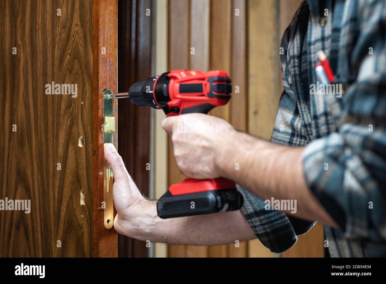 Close-up. Carpenter with an electric screwdriver fixes the lock of a ...