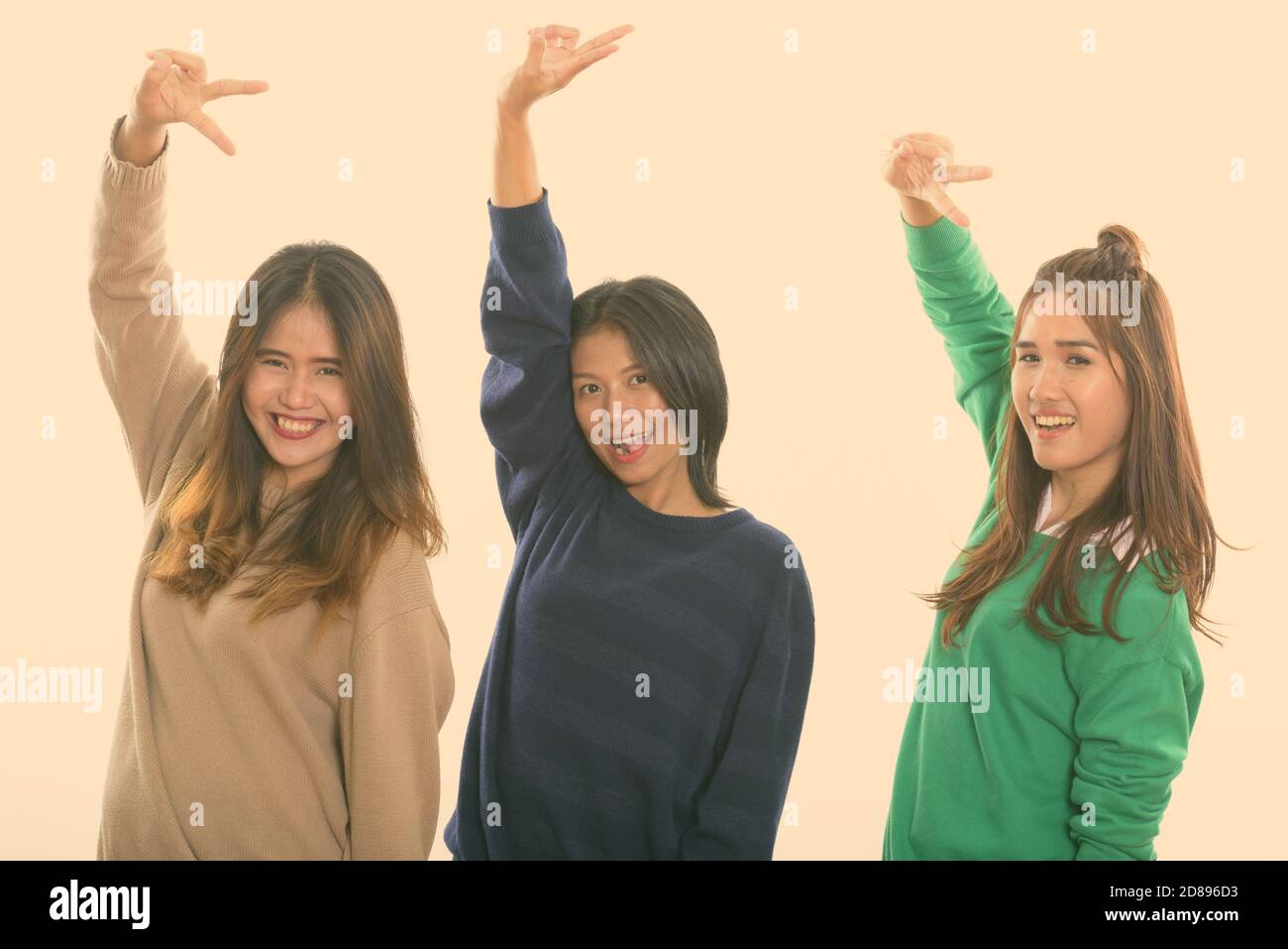 Studio shot of three happy young Asian woman friends smiling while ...