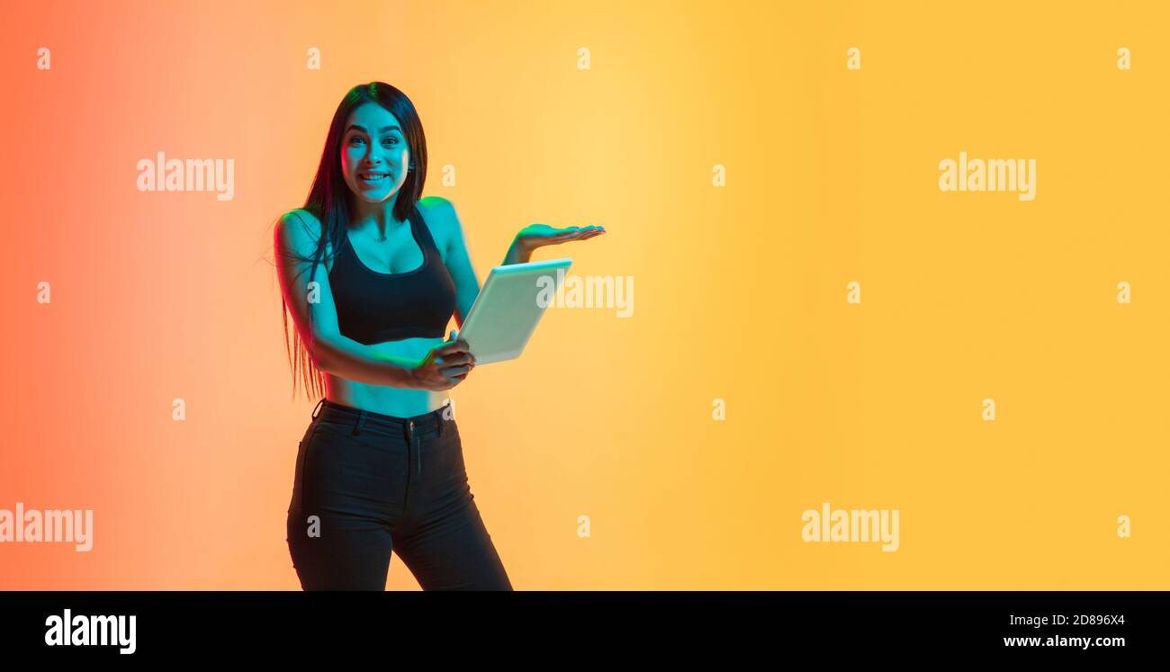 Scrolling tablet. Young caucasian woman's portrait on gradient yellow ...