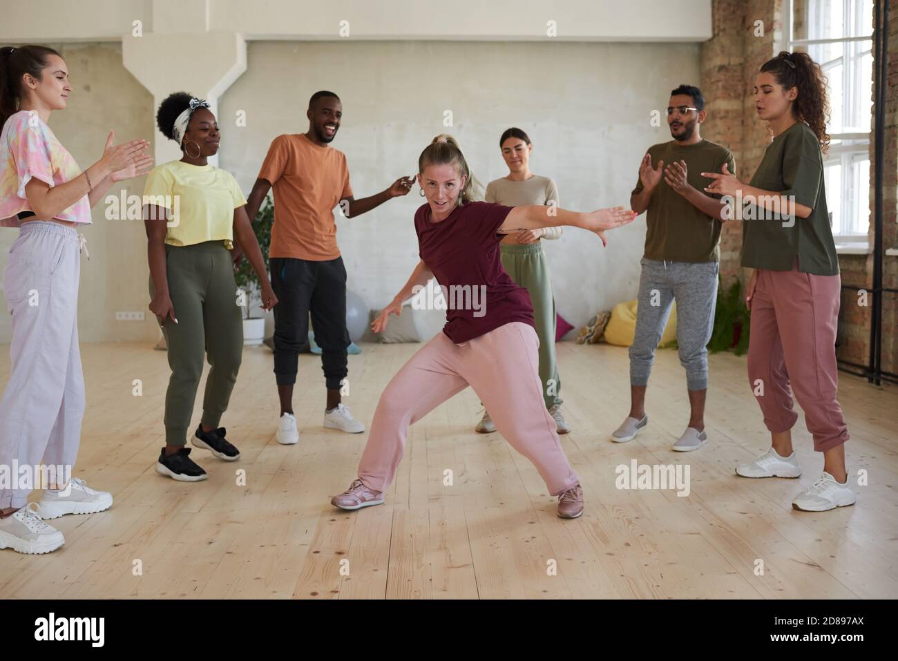 Young woman showing dance exercises while other people standing in ...
