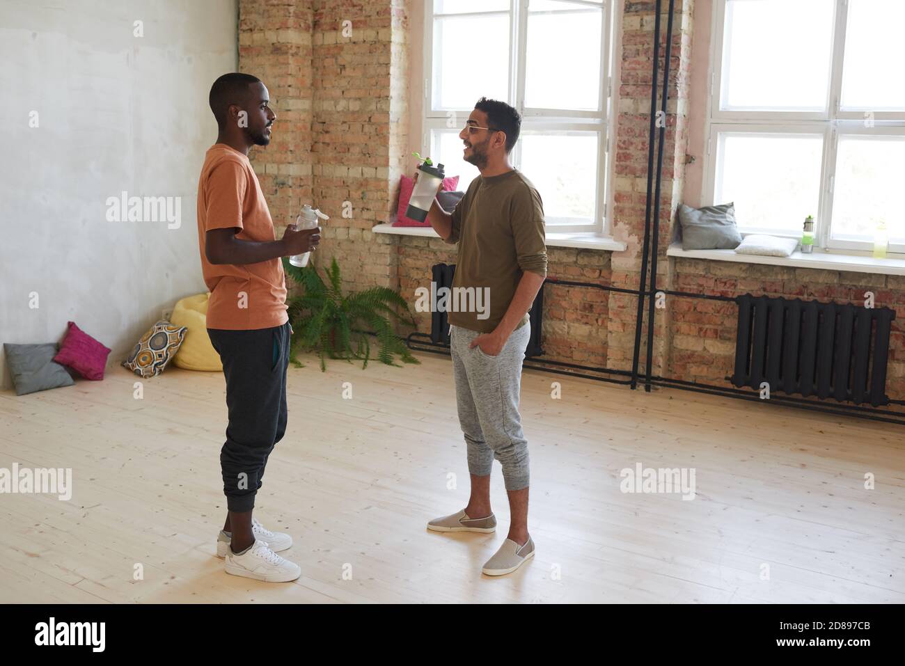 Two young men drinking water and talking to each other while standing ...