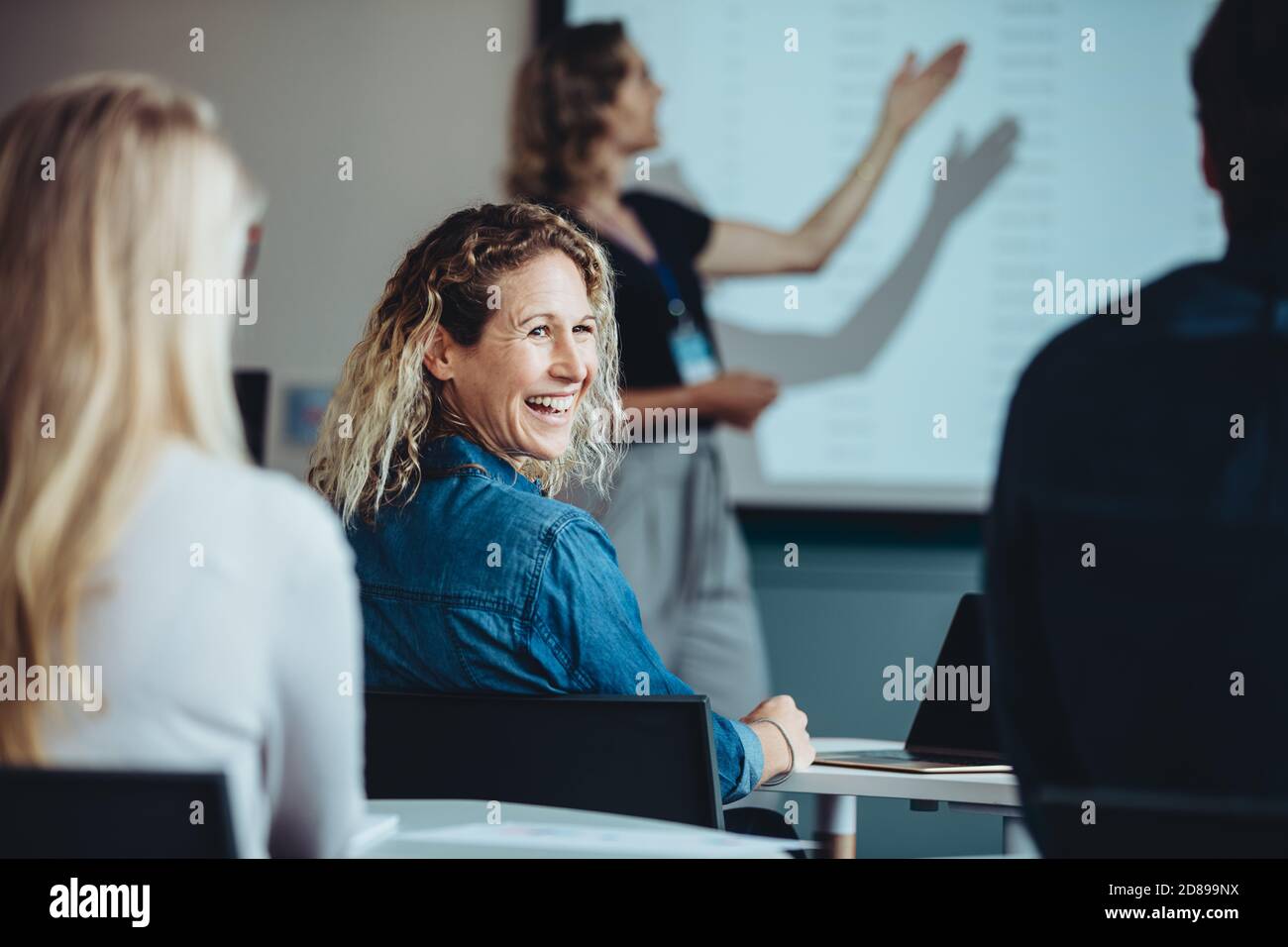 Rear view of a woman sitting in audience looking back at a colleague ...