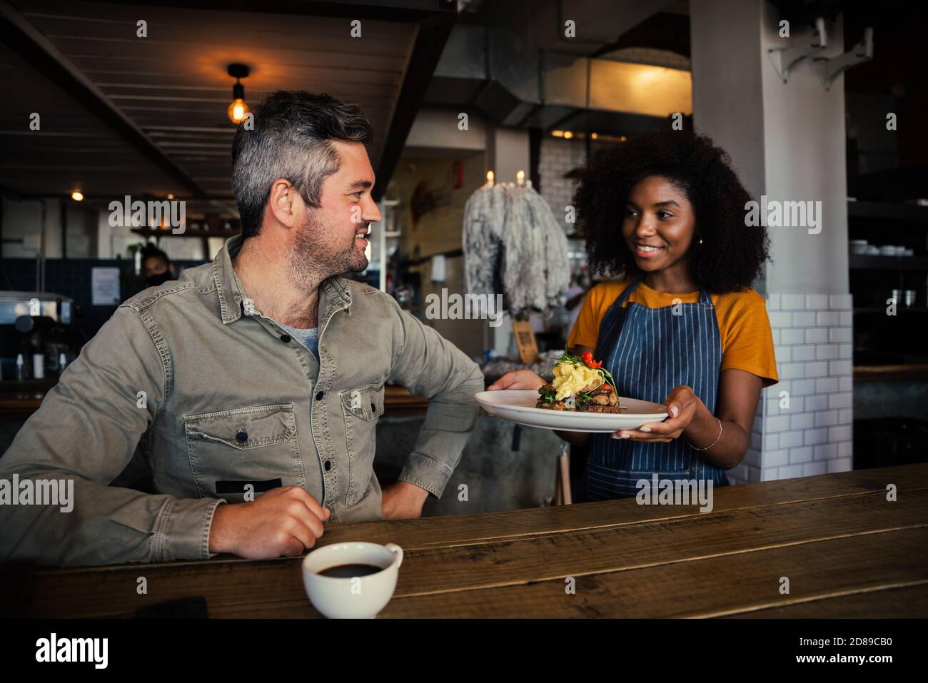 Smiling waitress serving male customer fresh egg breakfast while he ...