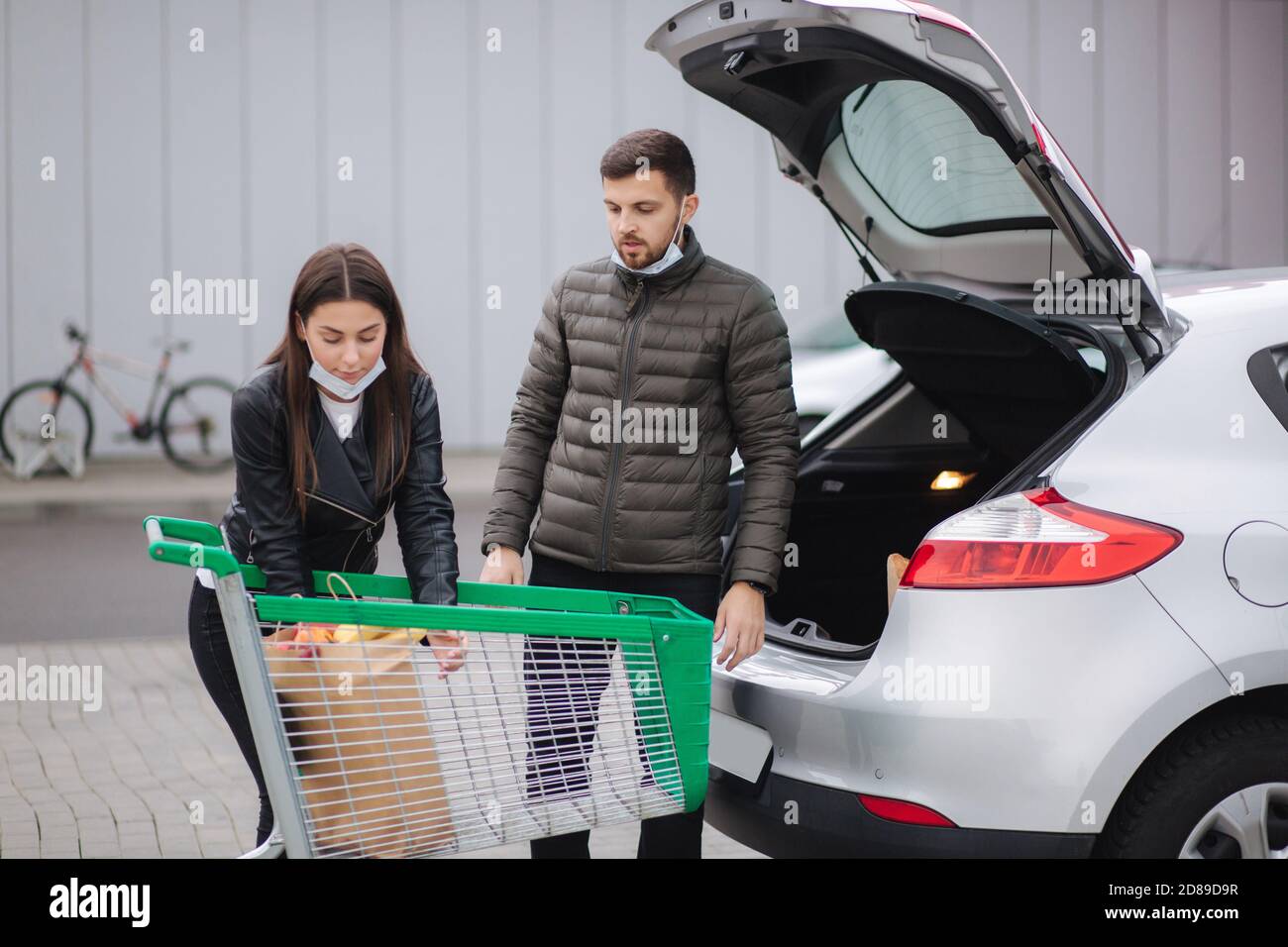 Young couple in masks loading bags in trunk after supermarket shopping ...