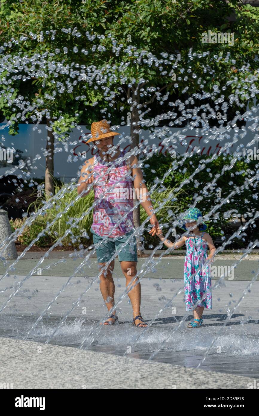 A young girl and her father playing together in the high arching water ...