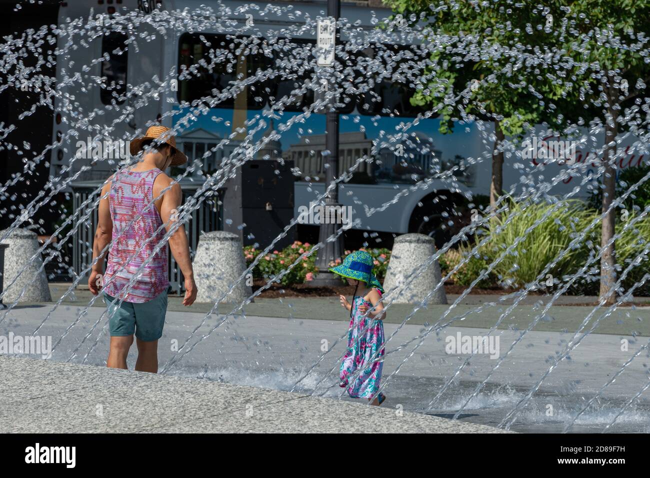 A young girl and her father playing together in the high arching water ...