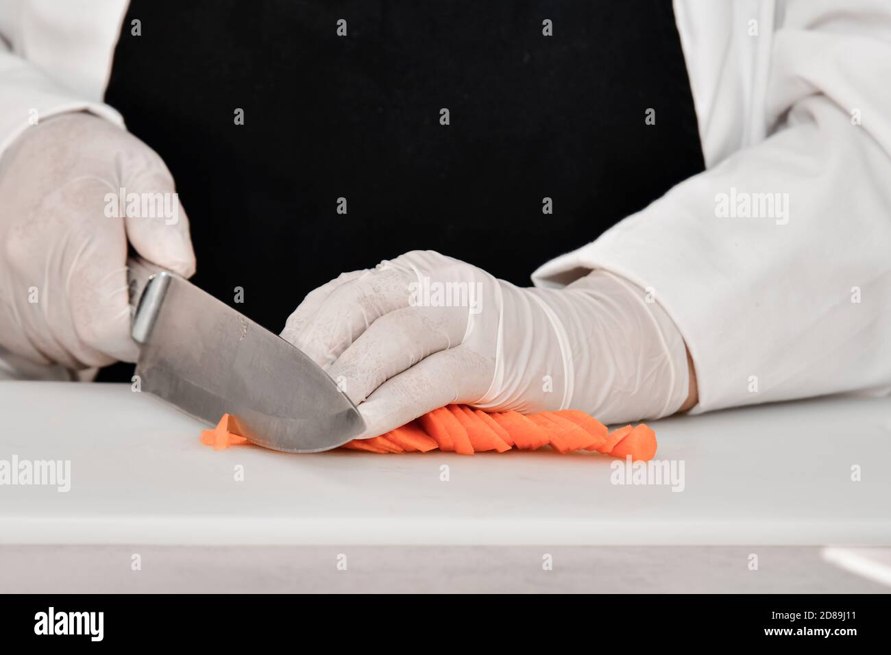 Close up of chef hands wearing gloves chopping a carrot with a kitchen ...