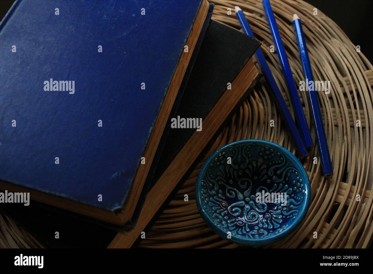 Blue books, pencils and a dish on a wicker table Stock Photo - Alamy