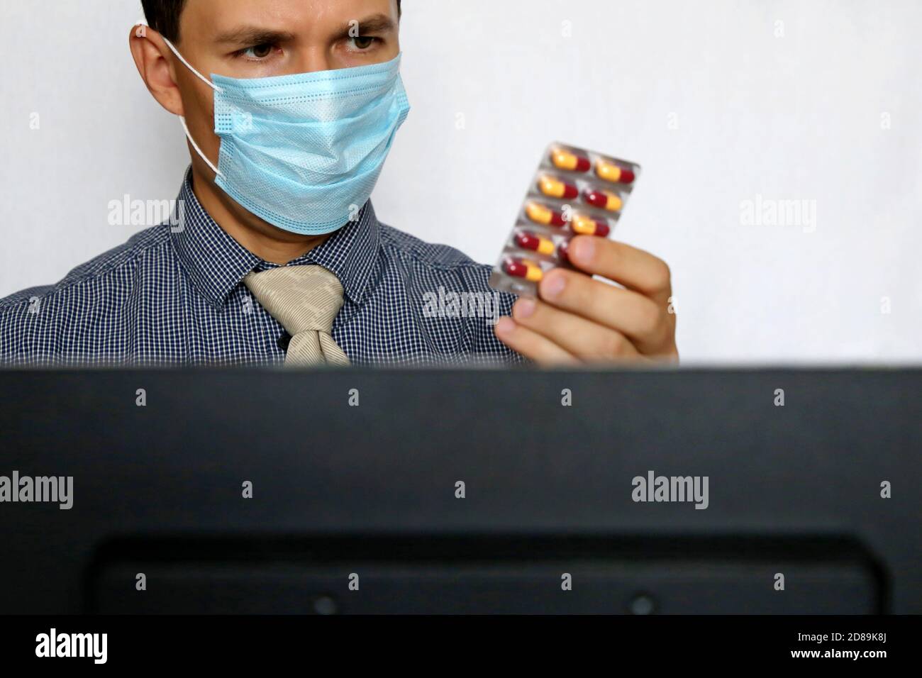 Man in face mask and office clothes looks at pills sitting at the PC ...