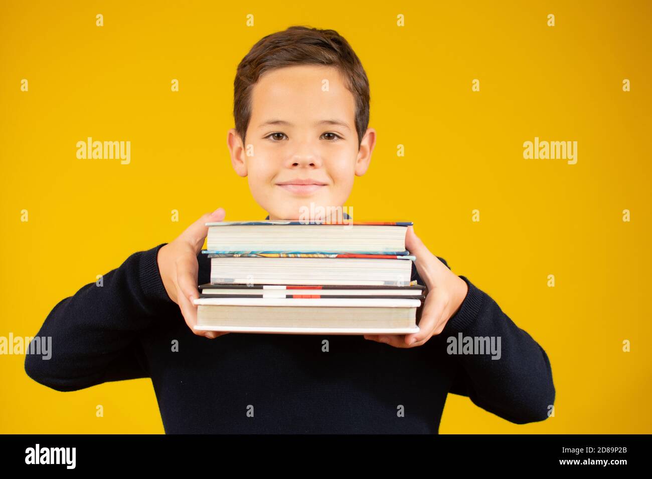 Happy smiling boy kid is holding in his hands many books over yellow ...