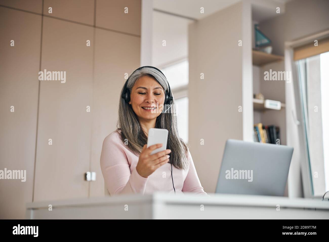 Elegant woman in pink sweater sitting at the white desk in room indoors ...