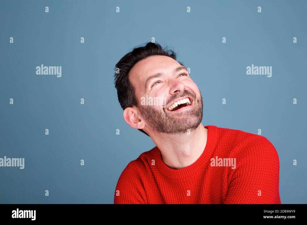 Close up portrait of happy man laughing and looking up against blue ...