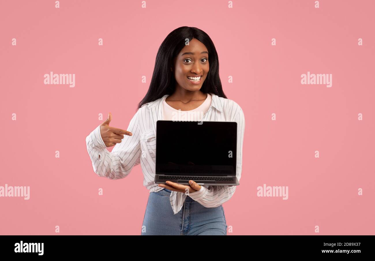 Happy black woman pointing at laptop with empty screen and smiling on ...