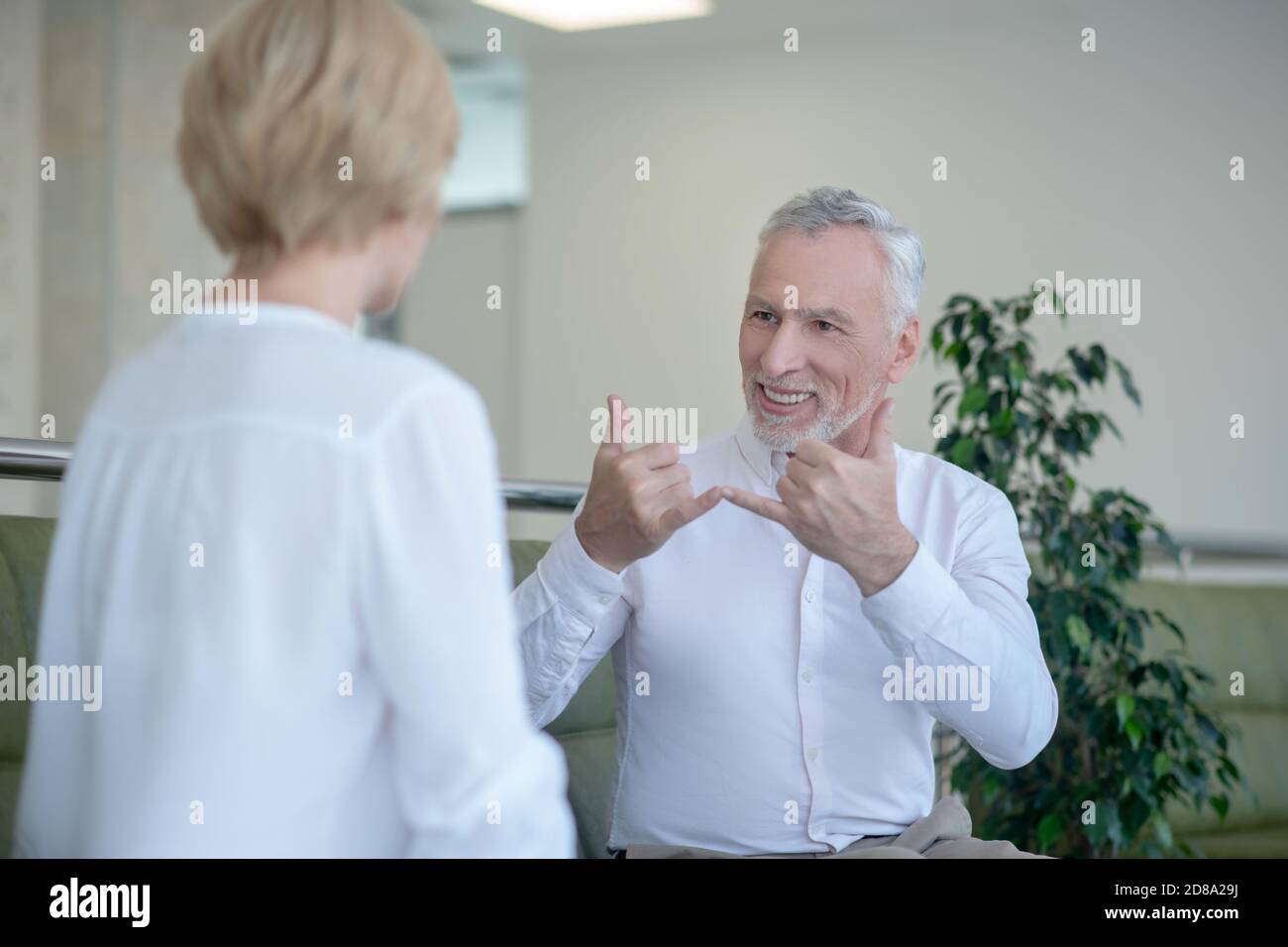 Bearded gray-haired man talking with blonde woman using sign language ...