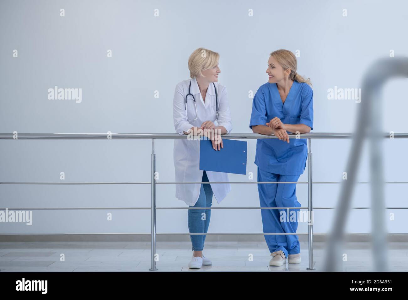 Two female doctors leaning on stair railing, discussing Stock Photo - Alamy