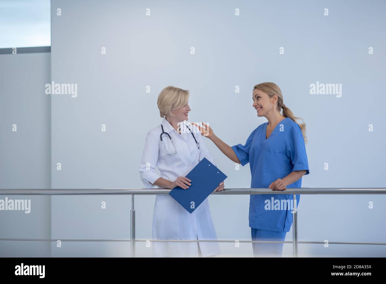 Two female doctors leaning on stair railing, having friendly ...